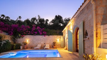 Piscina com espreguiçadeiras, parede de pedra e plantas em vasos.