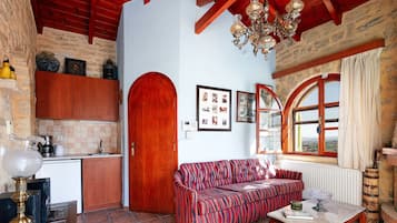 Uma sala de estar aconchegante com sofá, mesa de jantar, lustre e área de cozinha com armários de madeira e painel de azulejos.