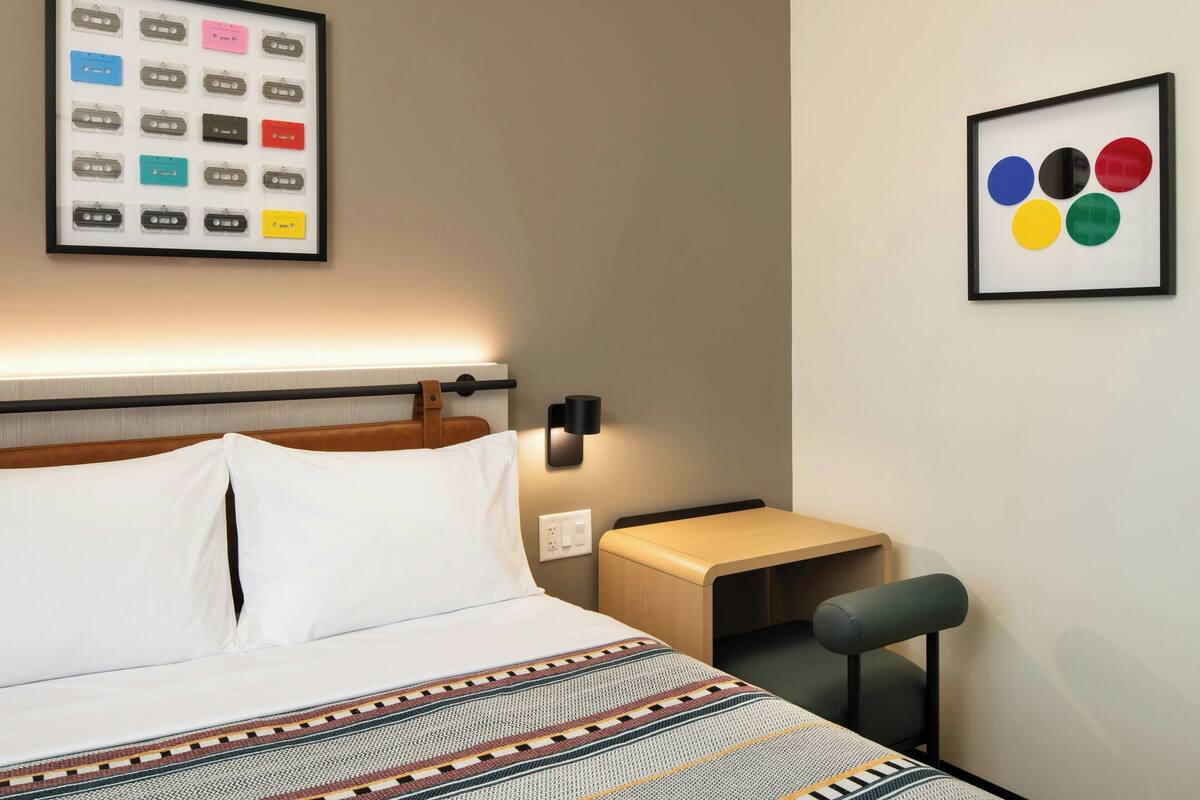 Quarto de hotel com cama, mesa de cabeceira, cadeira, luminária na parede e duas fotos emolduradas.