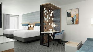 Quarto de hotel com duas camas, uma mesa, uma cadeira e um sofá.