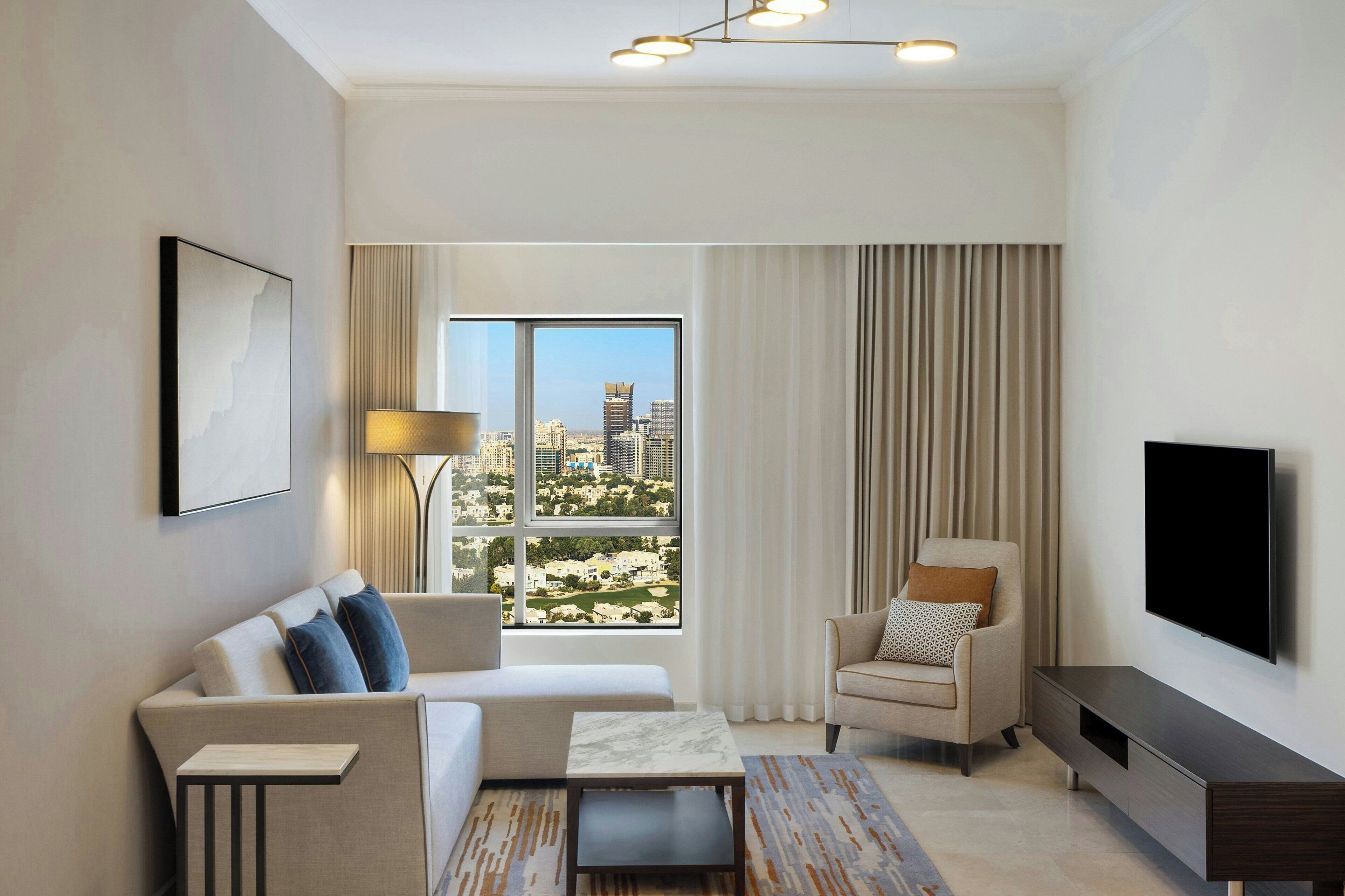 Quarto de hotel moderno com sofá, poltrona e televisão na parede.