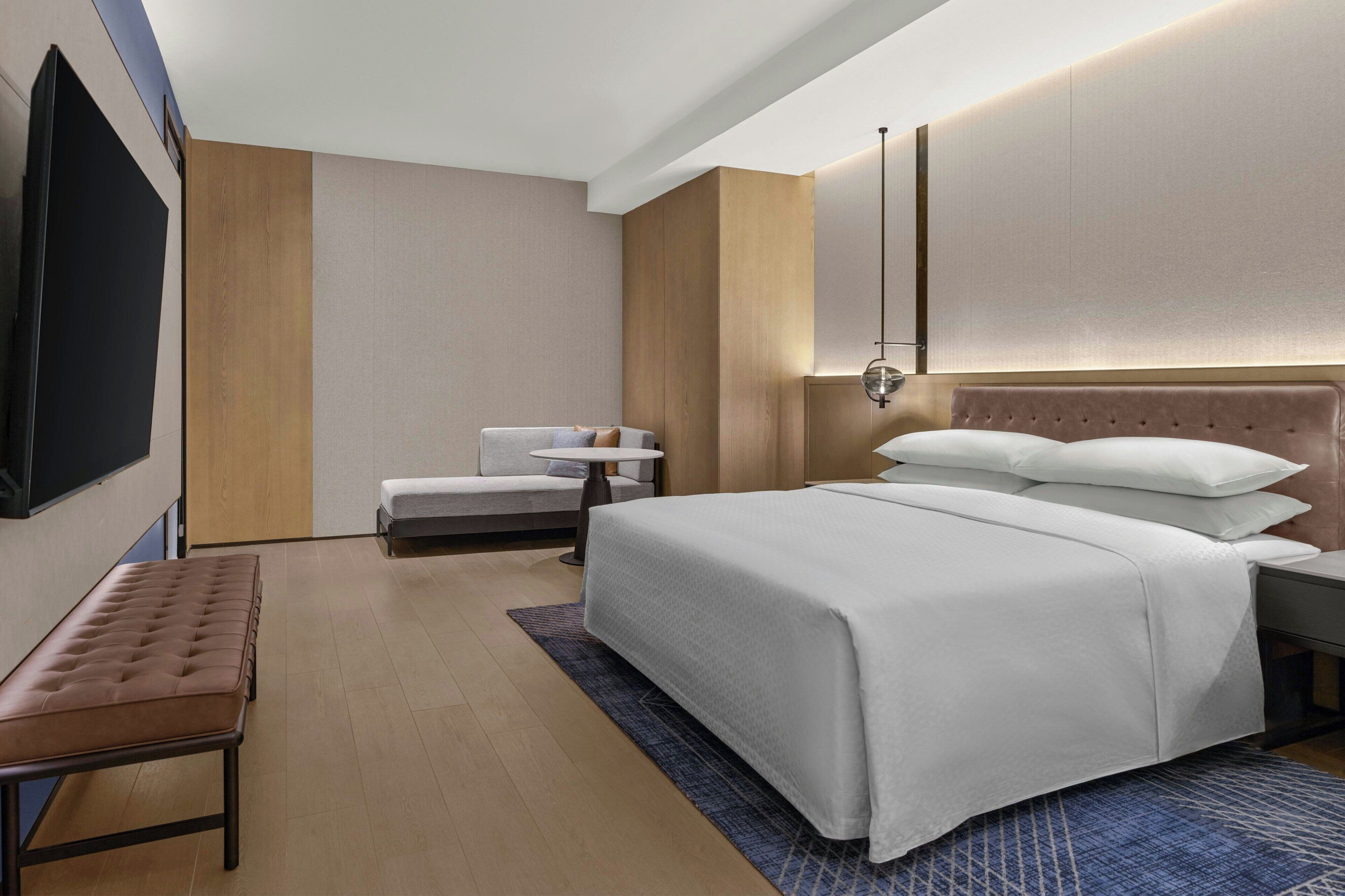 Quarto de hotel moderno com uma cama grande, um banco, uma mesa pequena e uma TV de tela plana.