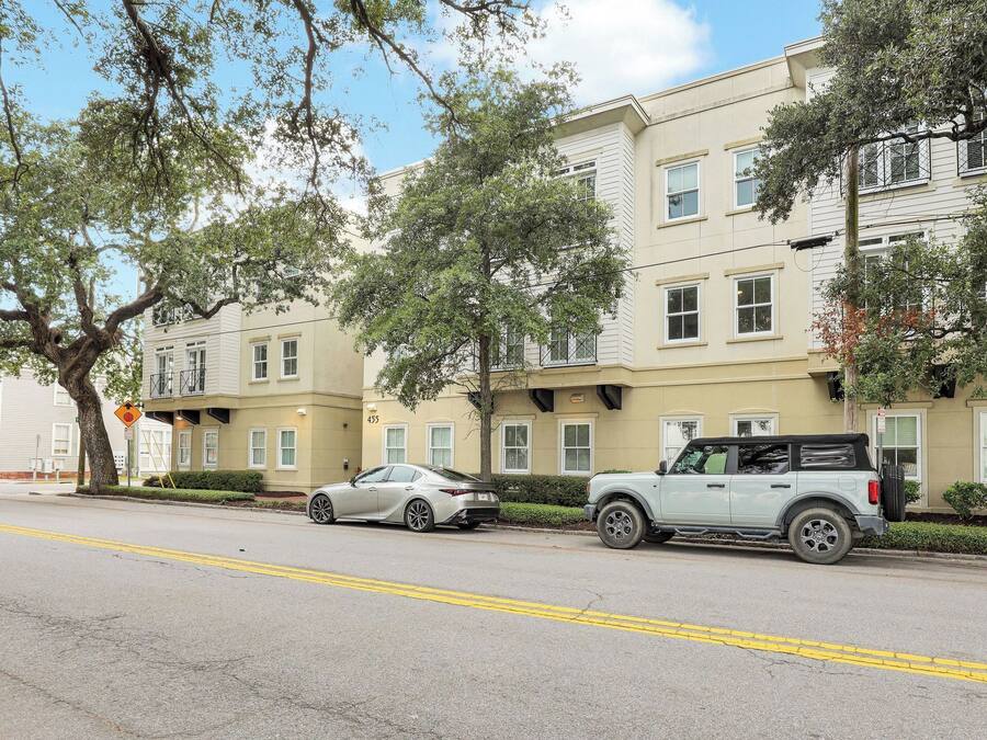 Um edifício residencial de vários andares com fachada bege, um carro sedã prata estacionado e um SUV branco na rua.