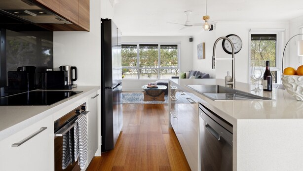 Cozinha moderna com ilha central, eletrodomésticos de aço inoxidável e vista para uma sala de estar.