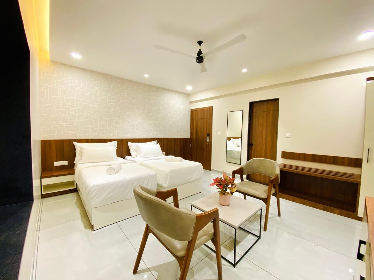 Quarto de hotel com uma cama, duas mesas de cabeceira, uma cadeira, uma mesinha e um espelho.