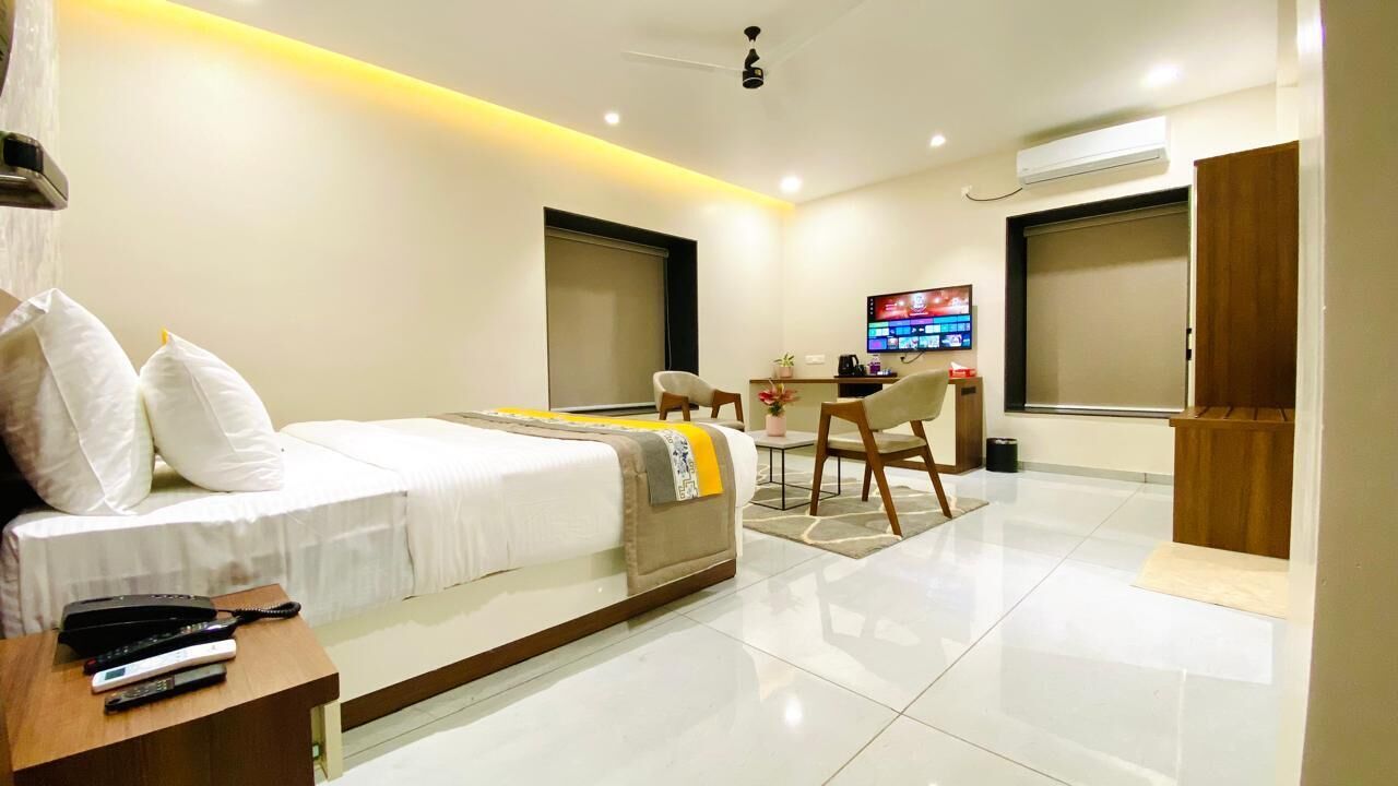 Quarto de hotel moderno com uma cama, escrivaninha, cadeira, televisão e guarda-roupa.