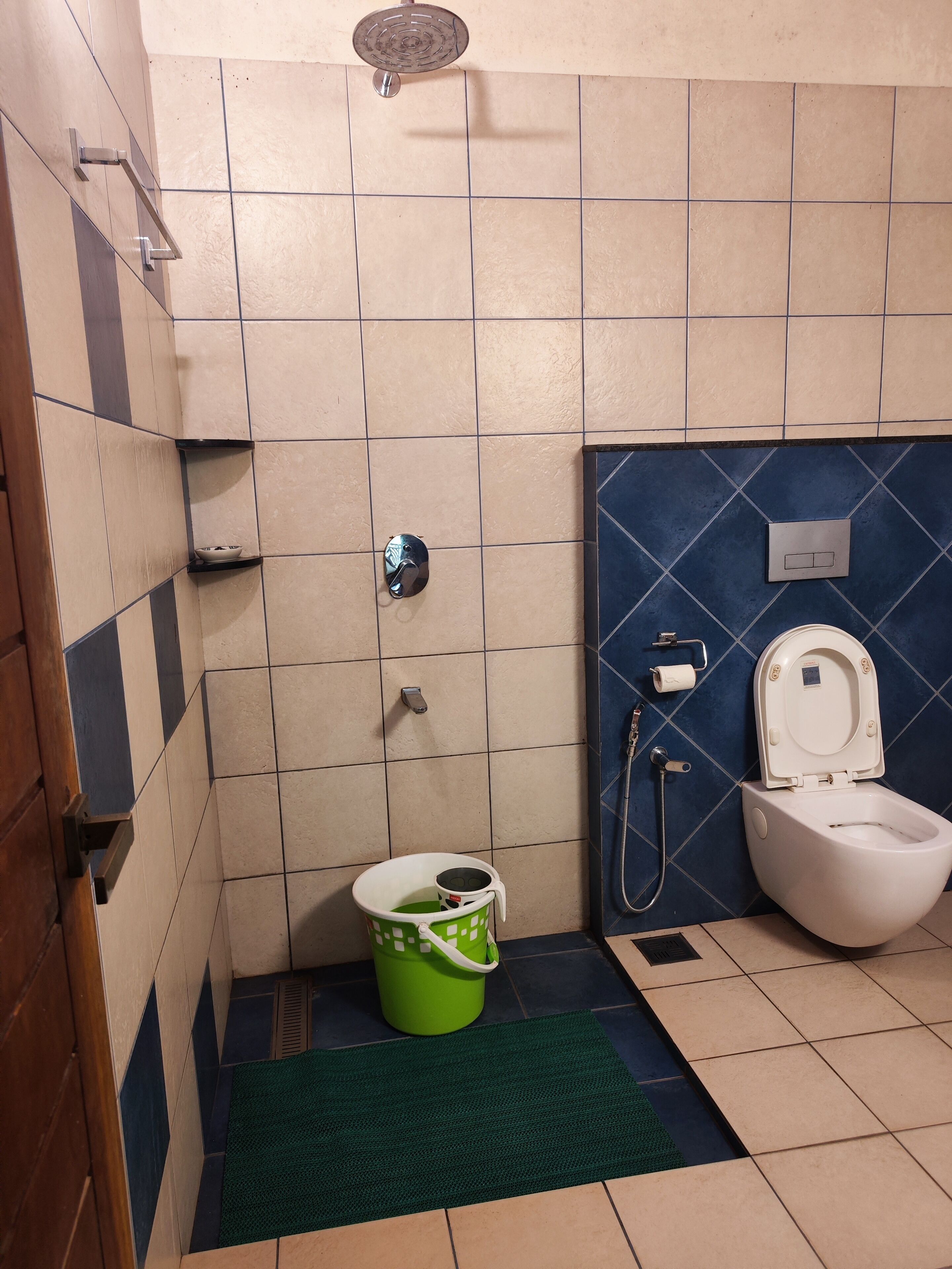 Um banheiro pequeno com vaso sanitário, chuveiro e um balde verde no chão.