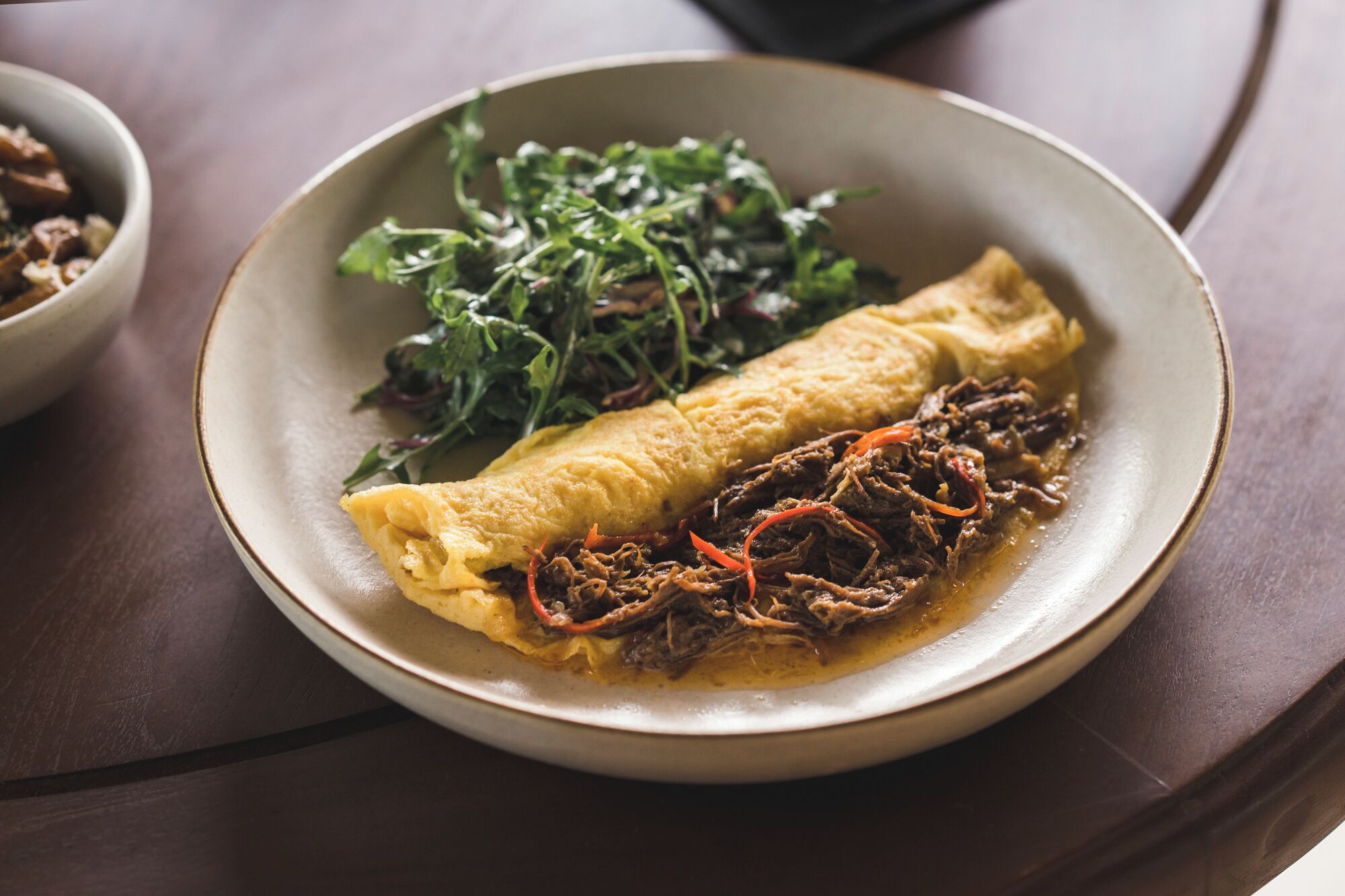 Um prato com omelete enrolada, carne desfiada e uma salada.