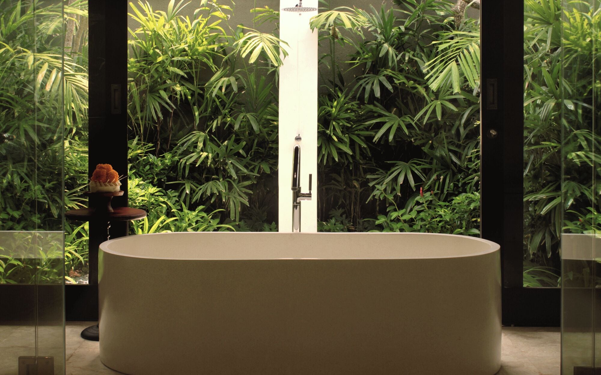 Casa de banho moderna com uma banheira grande, rodeada por plantas verdes exuberantes.