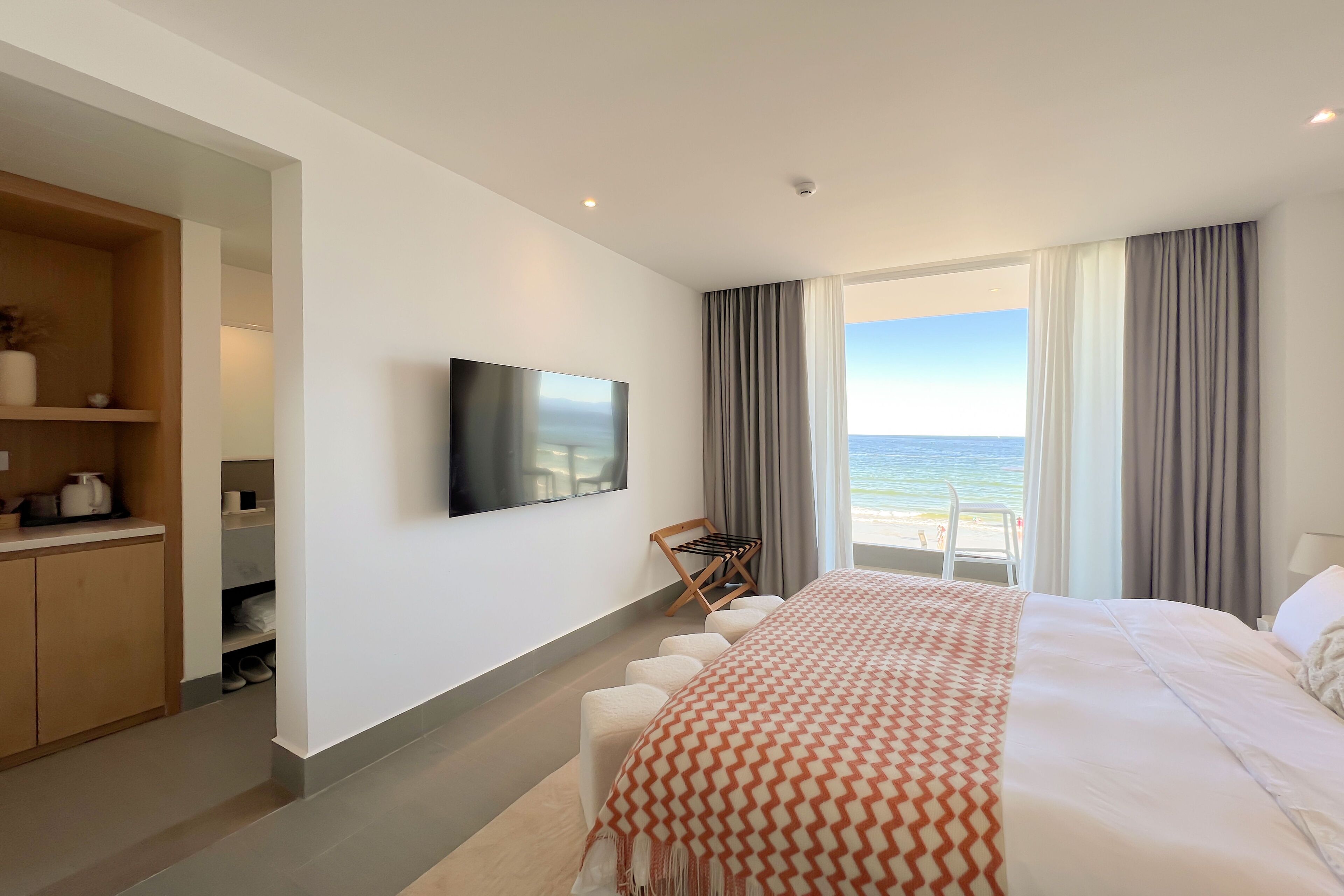 Quarto de hotel com cama, televisão, vista para o mar e cozinha compacta.