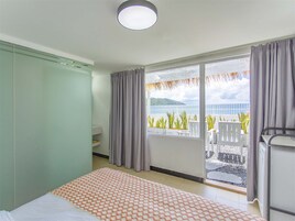 Quarto de hotel com cama, uma mesinha, uma cadeira e varanda com vista para o mar.