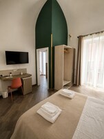 Quarto de hotel com cama, escrivaninha, televisão e guarda-roupa.