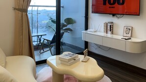 Uma sala de estar moderna com sofá, mesa de centro, televisão na parede e vista da cidade por uma porta de vidro.