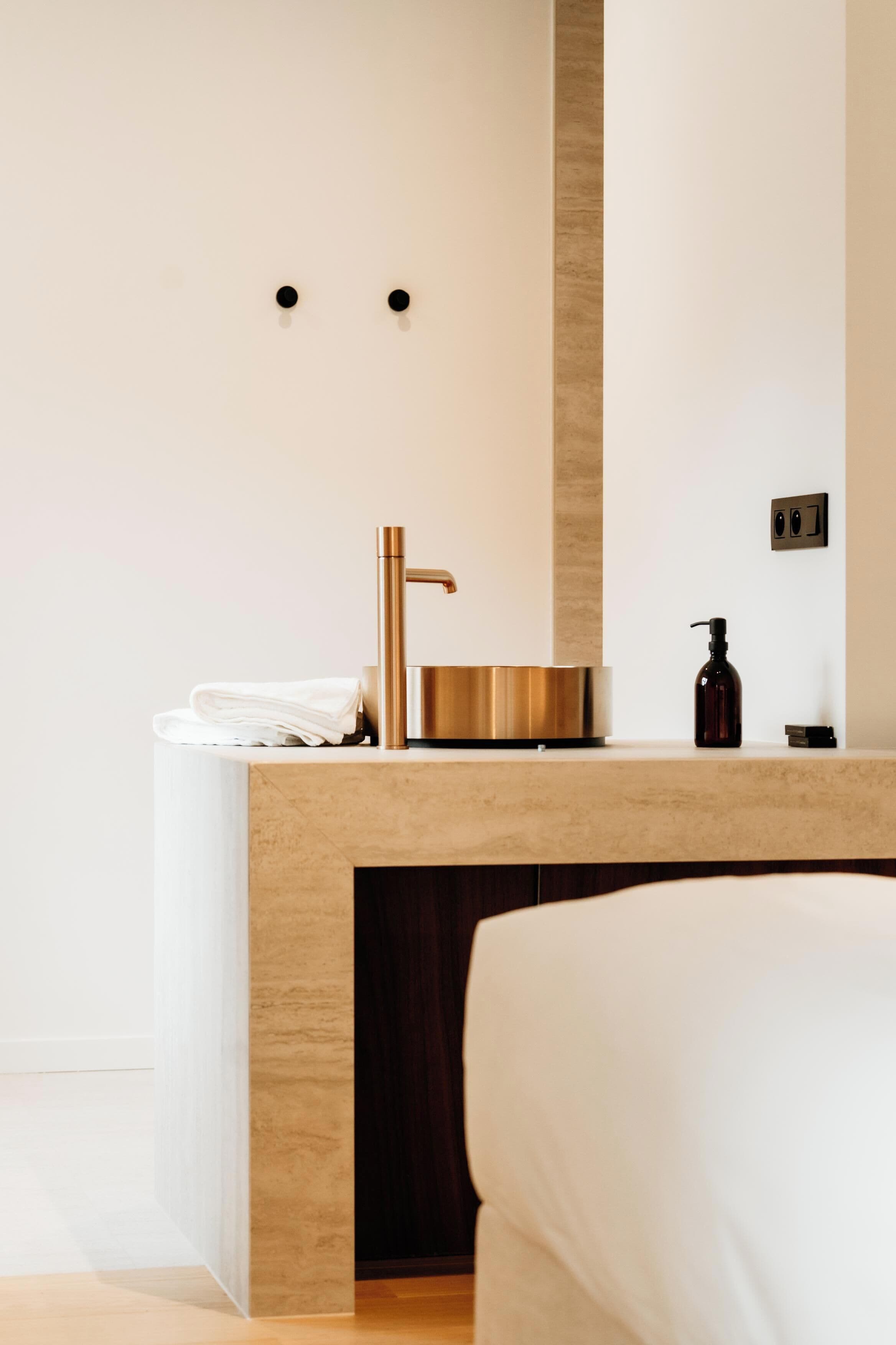 Casa de banho moderna com design minimalista, apresentando uma toucador de madeira, uma torneira dourada e uma pia branca.