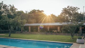 Piscina com deck de pedra, área de varanda coberta e edifício de pedra com telhado de metal.