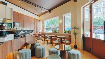Interior de café com balcão, mesas e grandes janelas.