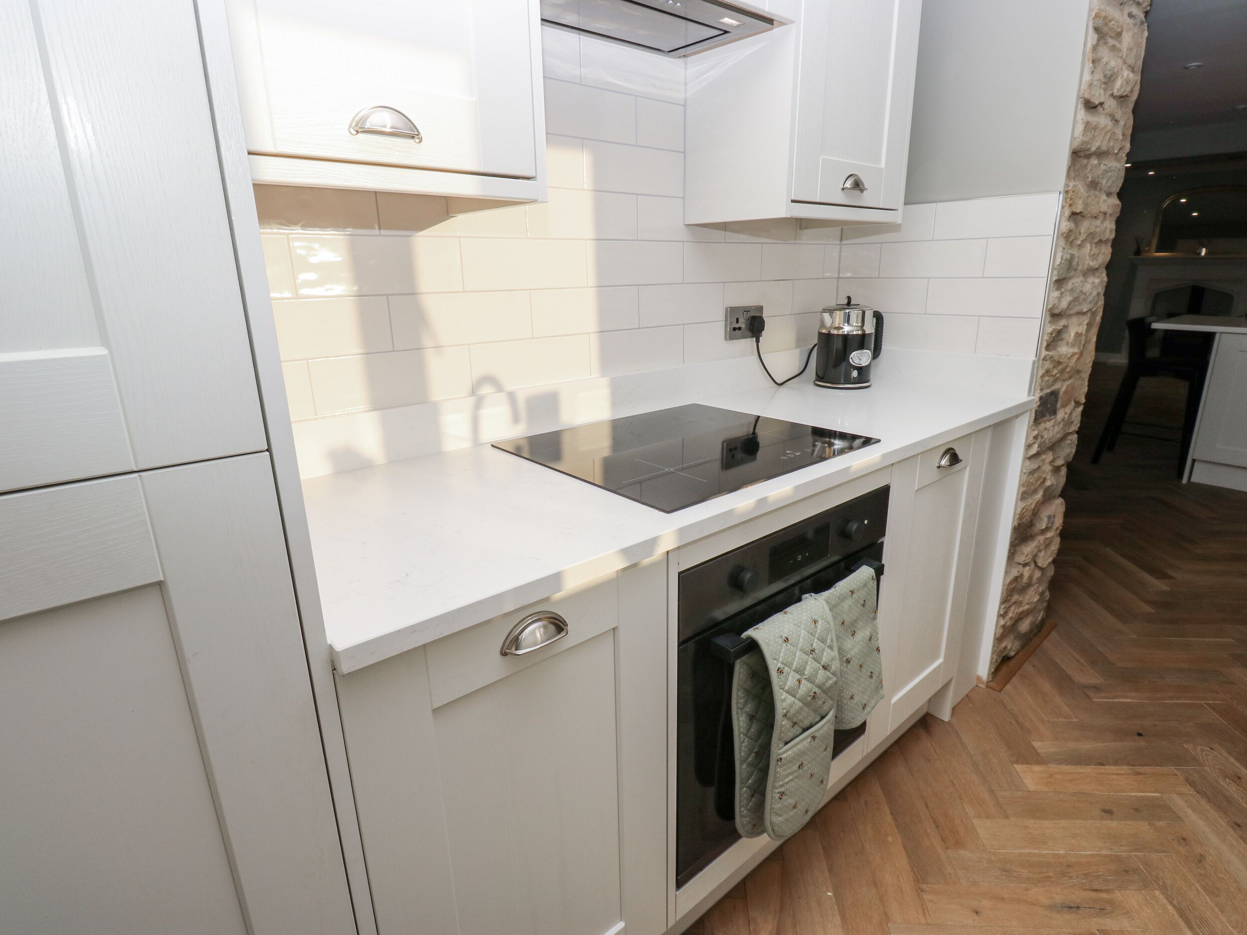 Uma cozinha com armários brancos, fogão preto e piso de madeira em padrão herringbone.