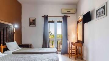 Quarto de hotel com duas camas, uma escrivaninha, uma cadeira, uma televisão e uma varanda com cortinas.