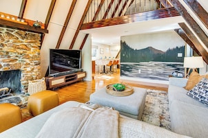 Uma sala de estar aconchegante com lareira de pedra, televisão de tela plana e uma grande pintura de uma paisagem montanhosa.