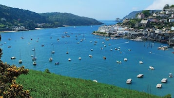 Uma vila costeira com vários barcos atracados em um porto, cercada por vegetação exuberante e colinas.