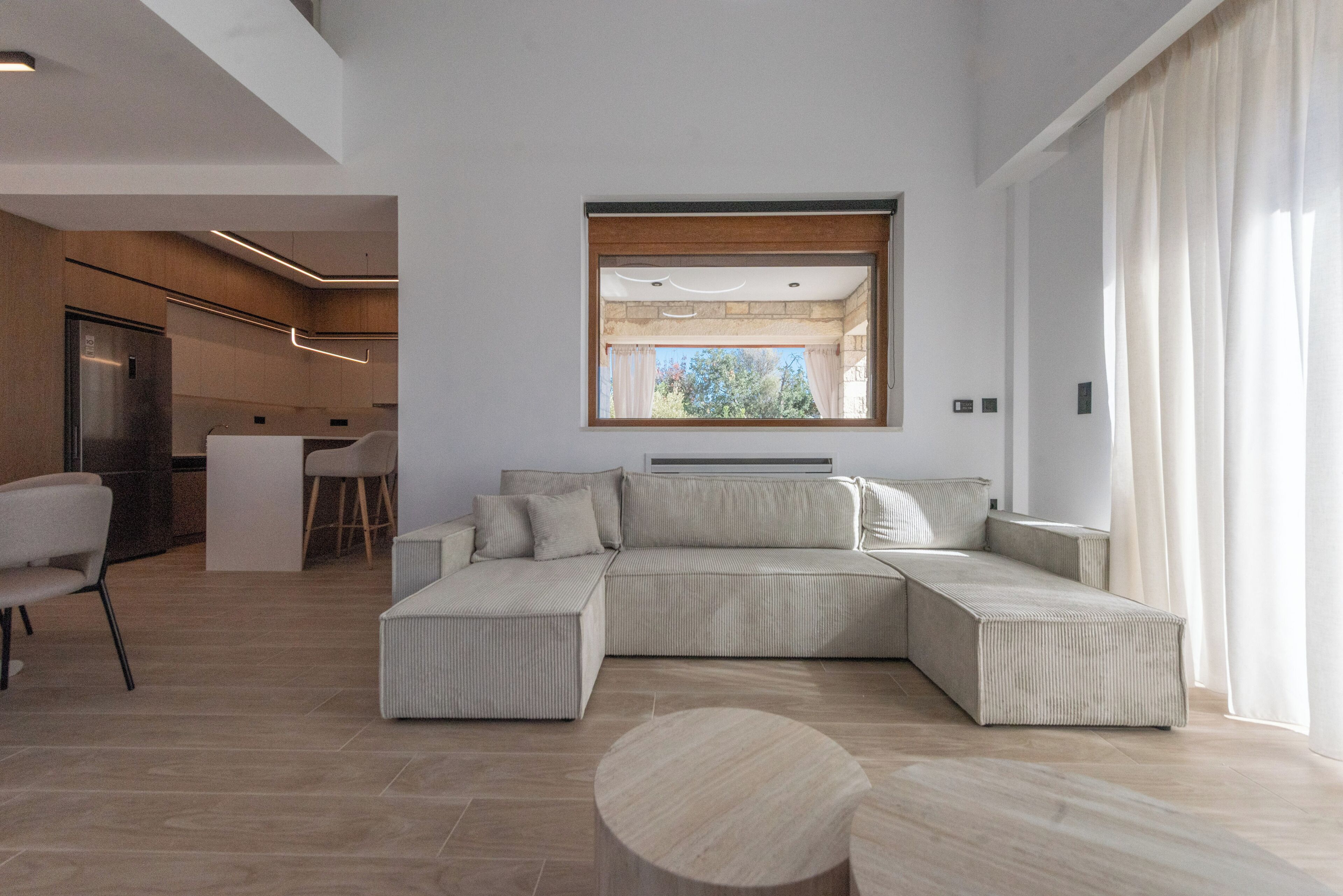 Uma sala de estar moderna com um sofá seccional, uma mesa de centro redonda de madeira e vista pela janela.