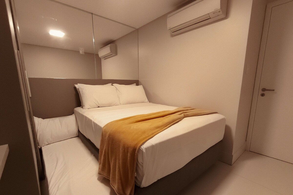 Uma cama de solteiro com cabeceira, mesa de cabeceira e unidade de ar condicionado na parede.