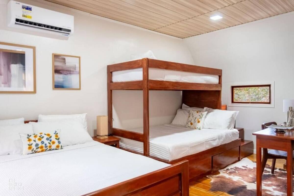 Quarto com uma cama de dossel de madeira, uma escrivaninha e duas fotografias emolduradas na parede.