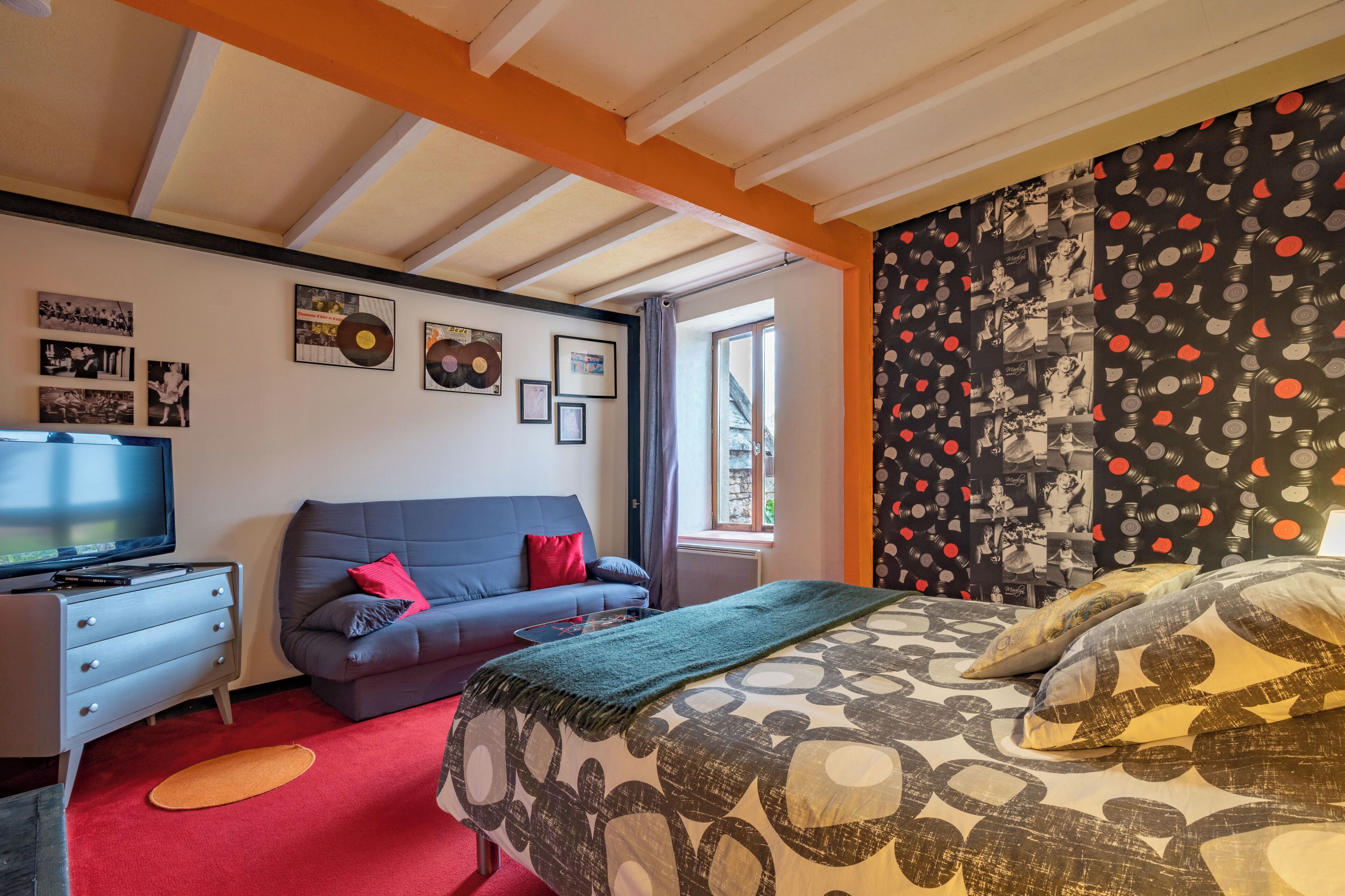 Quarto com cama, sofá, televisão e cômoda.