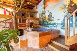 Uma banheira de hidromassagem com um banco de madeira, cercada por paredes de pedra e um mural com cena tropical.