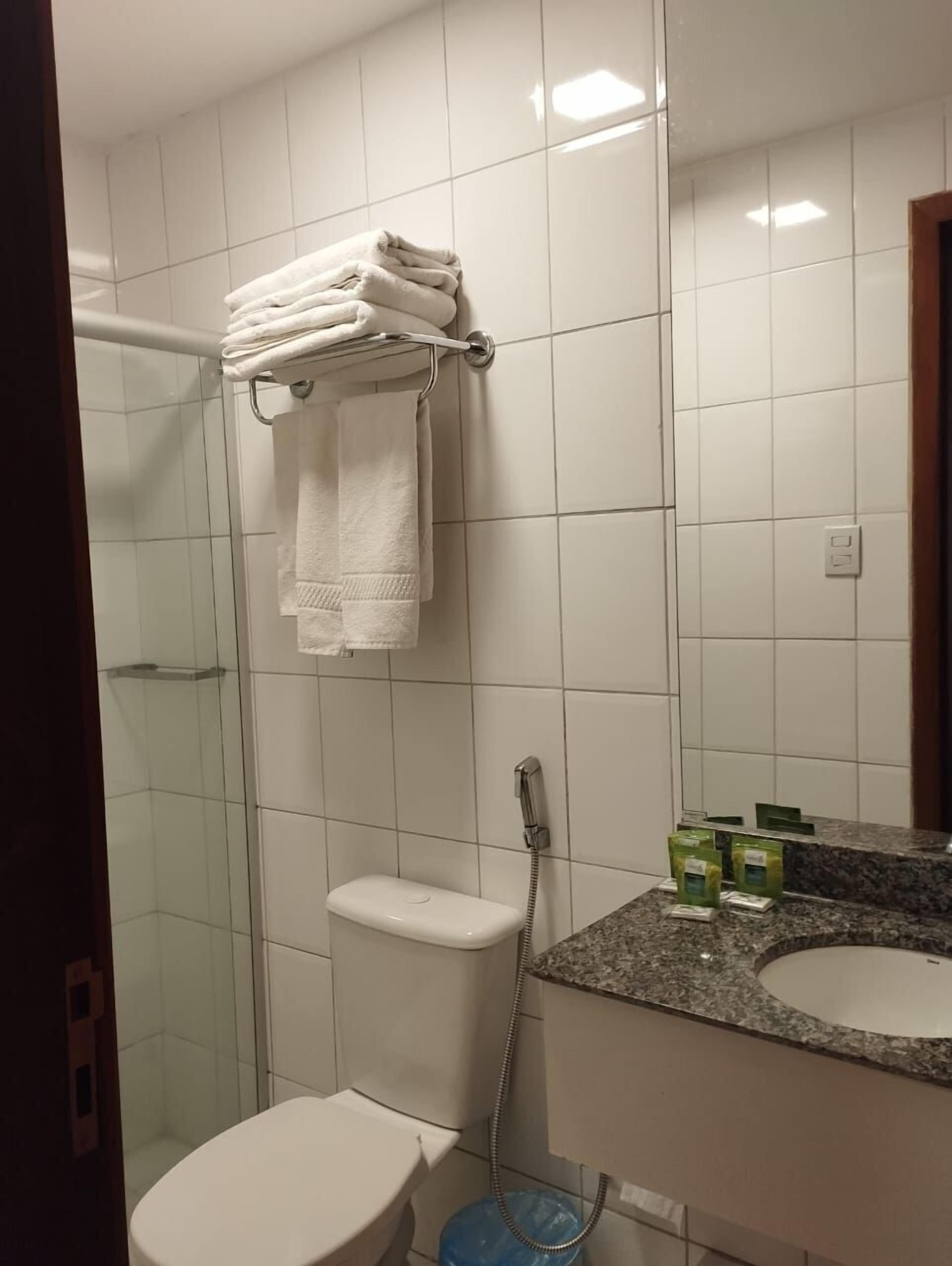 Um banheiro com vaso sanitário, chuveiro e pia com bancada de granito.