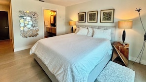 Um quarto espaçoso com uma cama grande, mesa de cabeceira com abajur e espelho decorativo na parede.