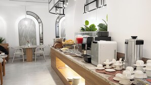 Um balcão de pequeno-almoço moderno com bancada de mármore, máquinas de café e diversas opções para o pequeno-almoço.