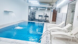 Uma piscina interior com água cristalina, um trampolim e cadeiras de descanso brancas.