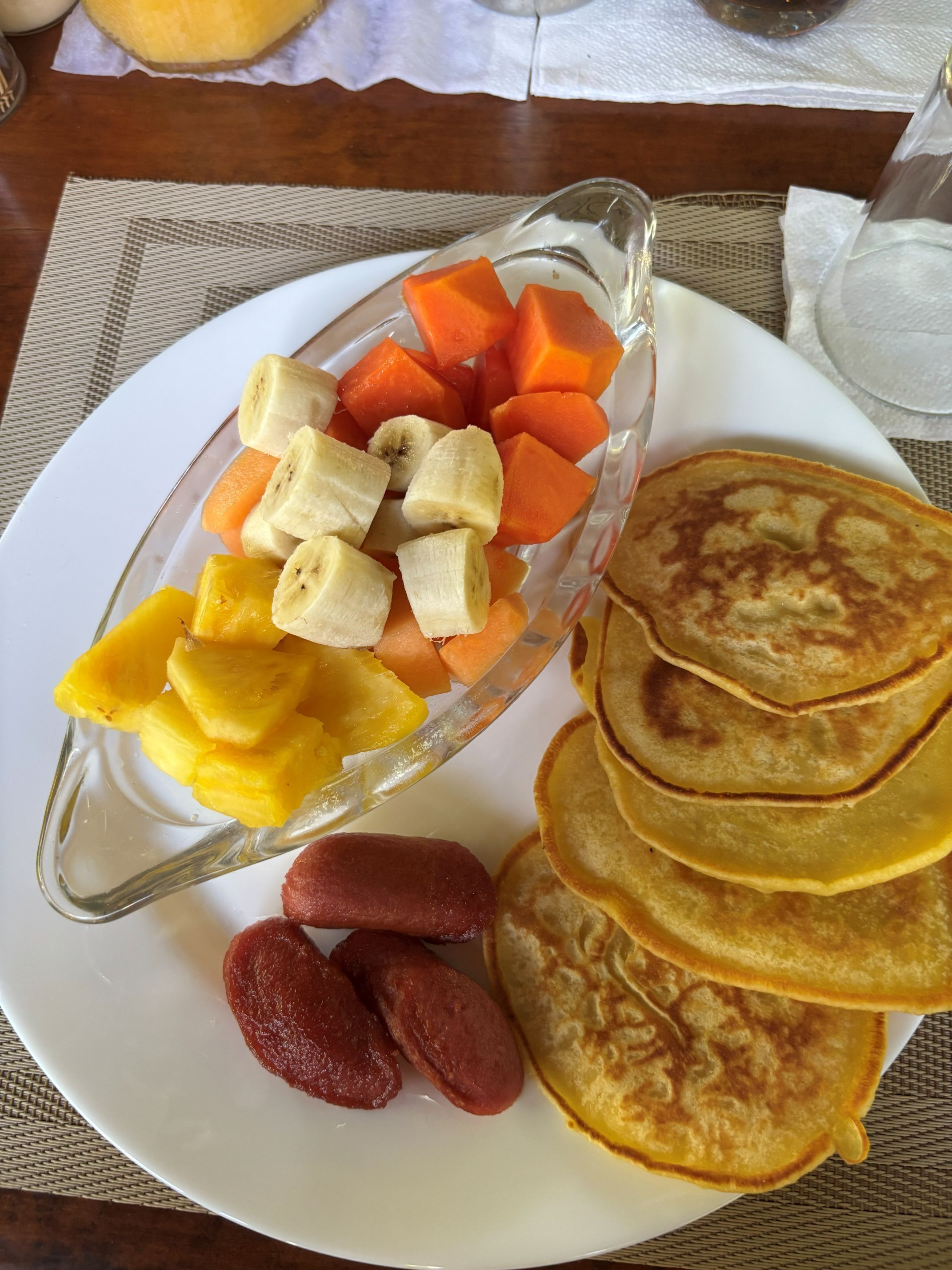Um prato com panquecas, fatias de banana, manga picada e feijão vermelho.
