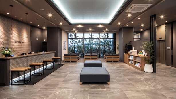 Um lobby moderno com balcão de recepção, área de estar e uma janela ampla com vista para o exterior.