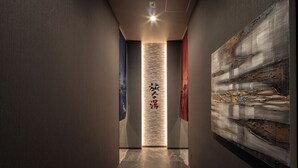 Um corredor moderno com piso de mármore, iluminação vertical e uma grande pintura abstrata à direita.