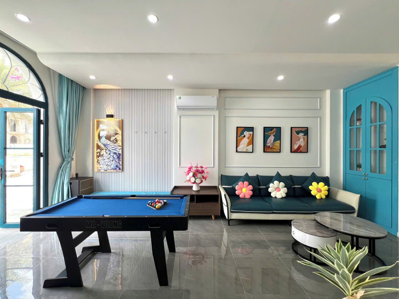 Uma sala de estar moderna com mesa de bilhar, um sofá com almofadas florais e um armário azul.