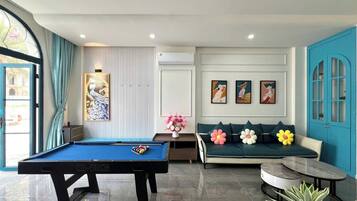 Uma sala de estar moderna com mesa de bilhar, um sofá com almofadas florais e um armário azul.