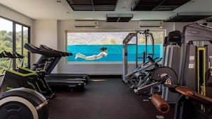 Uma academia com equipamentos de ginástica, esteira e uma grande janela com vista para um lago e árvores.