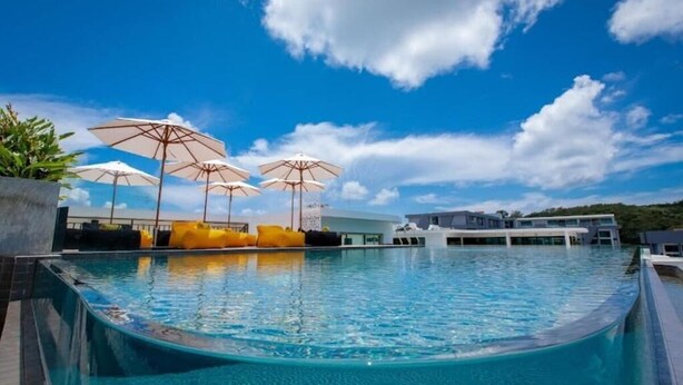 Piscina com vários guarda-sóis, um edifício moderno ao fundo e um céu azul límpido.