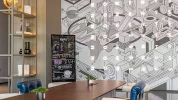 Uma sala de reunião moderna com uma mesa comprida, cadeiras azuis, uma estante de livros e um cardápio em lousa.