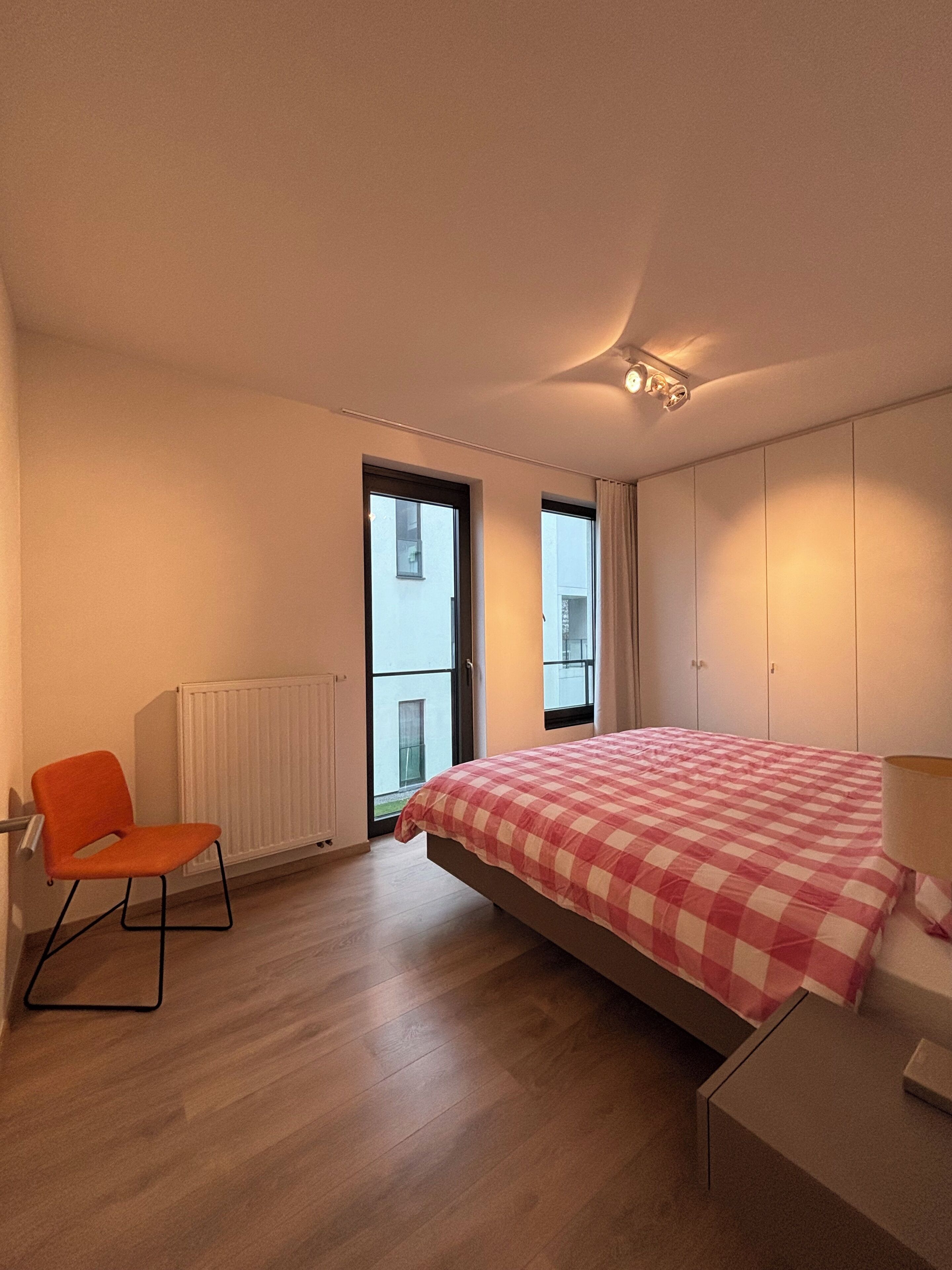 Quarto com cama, uma cadeira, radiador e janela.