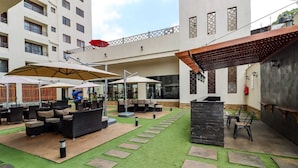 Um terraço no telhado com área de estar externa, churrasqueira e vista para edifícios vizinhos.
