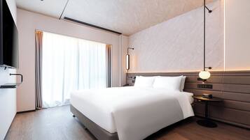 Quarto de hotel moderno com uma cama grande, televisão de tela plana, mesa de cabeceira, abajur e uma janela ampla com cortinas.