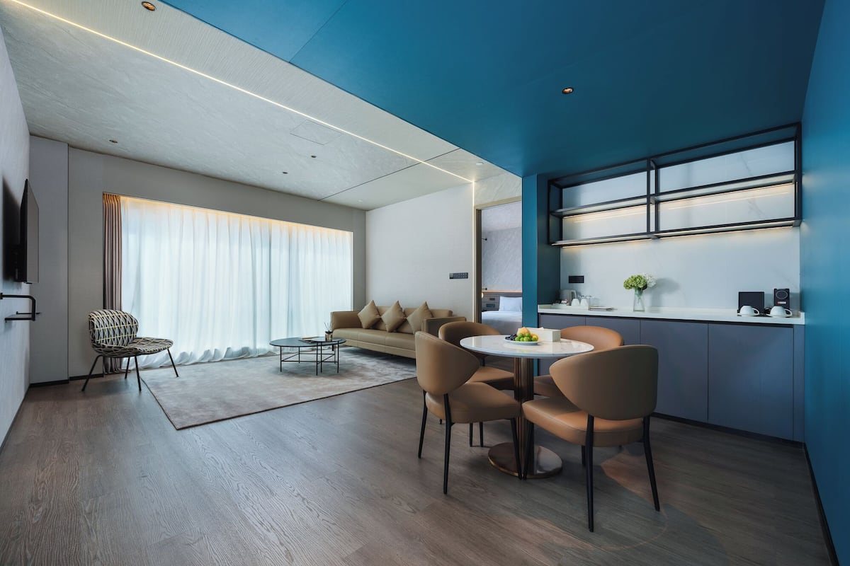Uma sala de estar moderna com um sofá, uma mesa de jantar com cadeiras e uma janela grande com persianas.