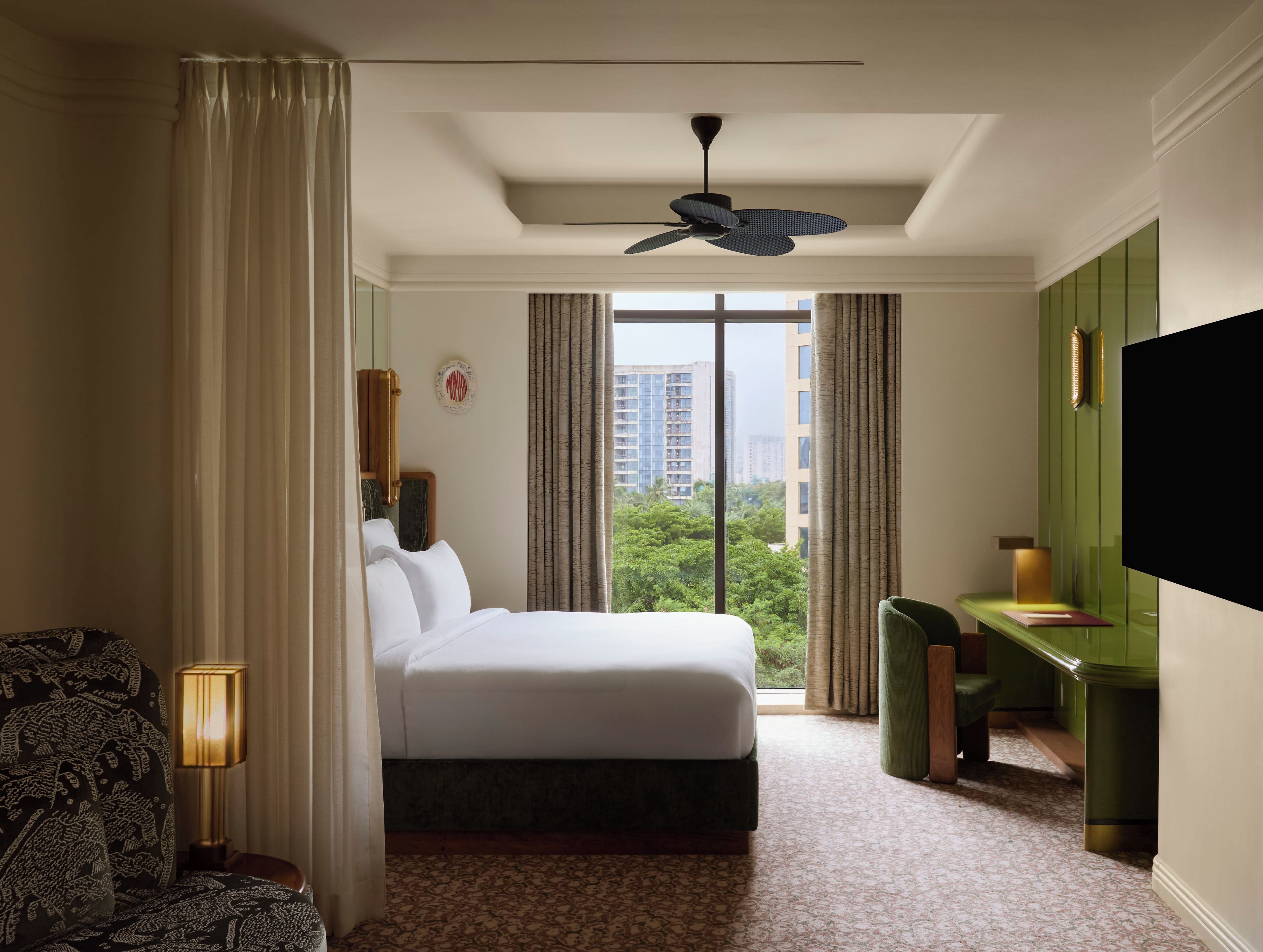 Quarto de hotel com cama, escrivaninha, televisão e vista para a cidade.
