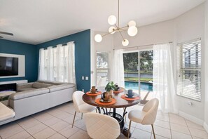 Uma sala de estar moderna com sofá, TV, mesa de jantar com cadeiras e vista para a piscina.