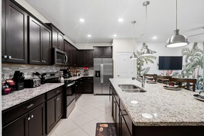 Uma cozinha moderna com armários escuros, eletrodomésticos de aço inoxidável, bancadas de granito e iluminação pendente.