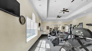 Academia com ventiladores de teto, equipamentos de ginástica e uma grande janela.