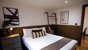 Quarto de hotel bem organizado com uma cama grande, mesas de cabeceira, uma cadeira suspensa e obras de arte nas paredes.
